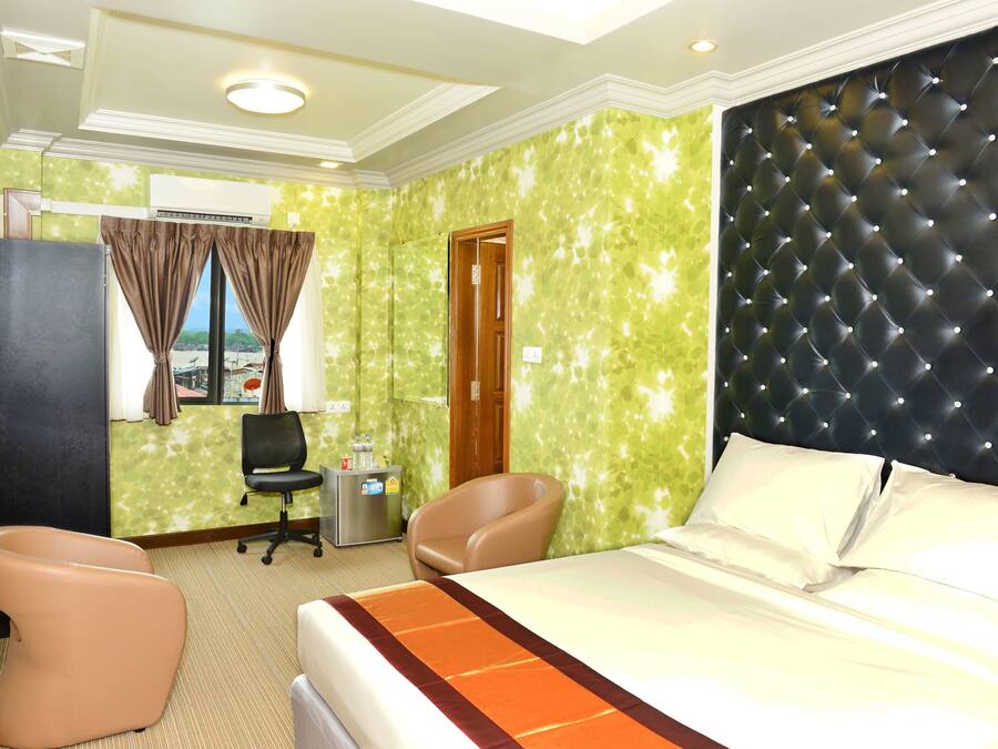 Quarto de hotel com cama, duas cadeiras, escrivaninha, ar condicionado e porta.