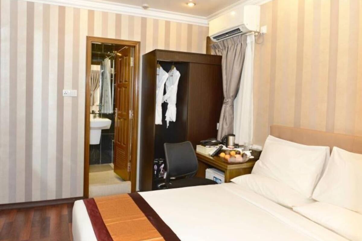 Quarto de hotel com cama, escrivaninha com cadeira, guarda-roupa e ar condicionado.