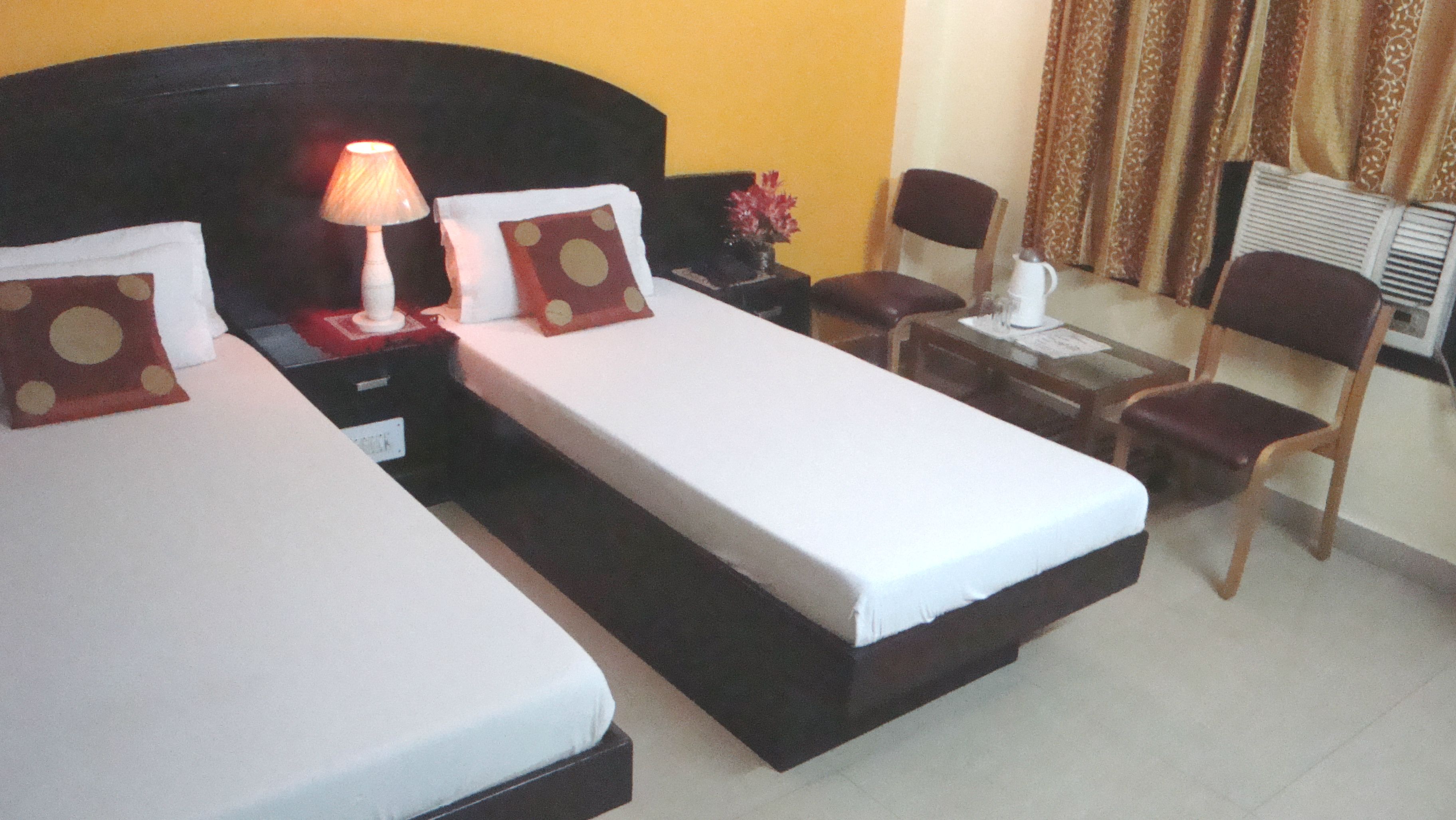 Quarto de hotel com duas camas, uma escrivaninha, uma cadeira, um abajur e uma janela com cortinas.