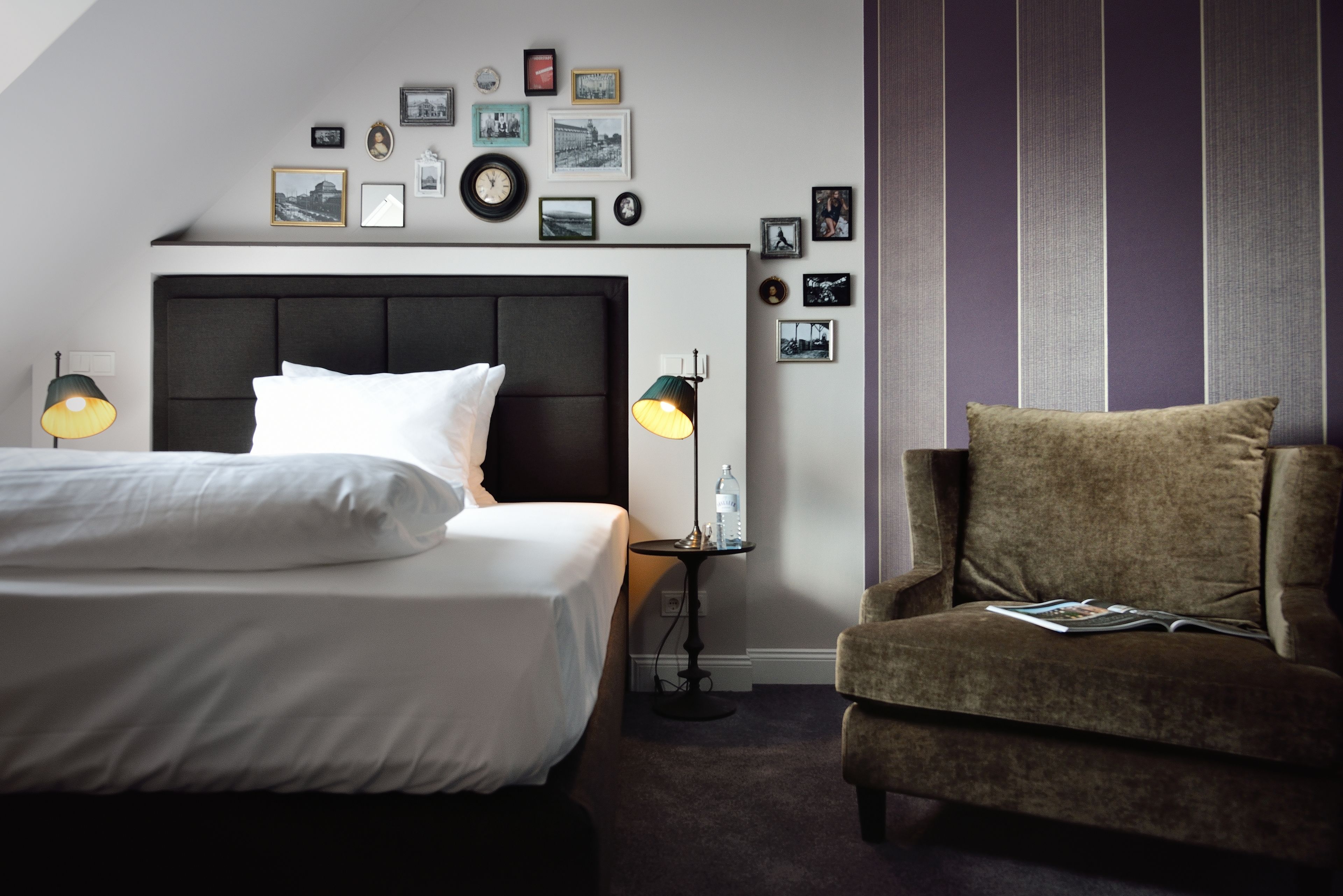 Quarto de hotel com cama, cadeira, mesa de cabeceira e parede decorada com quadros.