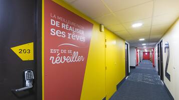 Corredor de hotel com parede em vermelho e amarelo, uma placa numérica e uma porta com fechadura eletrônica.