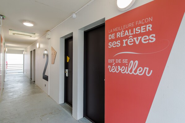 Um corredor com portas e uma placa vermelha com texto branco.