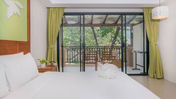 Quarto de hotel com uma cama grande, mesa de cabeceira com uma planta e vista para uma varanda com grades de madeira.