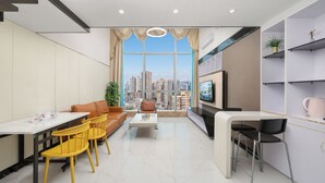 Uma sala de estar moderna com vista para a cidade, área de jantar com cadeiras amarelas, sofá marrom e cozinha com televisão e estantes.