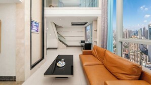 Uma sala de estar moderna com um sofá, uma mesa de centro e vista para a cidade através de amplas janelas.