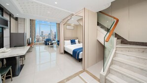 Quarto de hotel moderno com cama, área de refeições, escada e vista para a cidade.