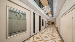 Corredor de hotel com piso estampado em padrão geométrico, paredes espelhadas e uma série de portas.