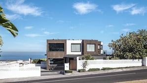 Uma casa moderna de dois andares com telhado plano, janelas amplas e cerca branca.