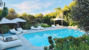 Uma piscina com espreguiçadeiras brancas e guarda-sóis, cercada por vegetação exuberante.
