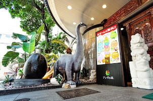 Uma estátua de dinossauro, uma esfera de pedra grande e uma estátua tradicional de leão chinês em um ambiente interno, com piso de azulejos e teto decorativo.
