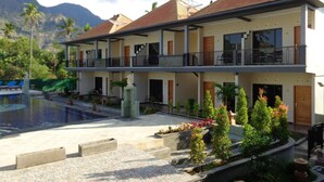 Um hotel de dois andares com piscina, área de estar externa e montanhas ao fundo.