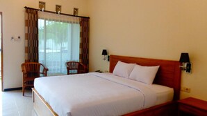 Quarto de hotel com uma cama grande, duas cadeiras, uma mesinha de cabeceira e uma janela com cortinas.