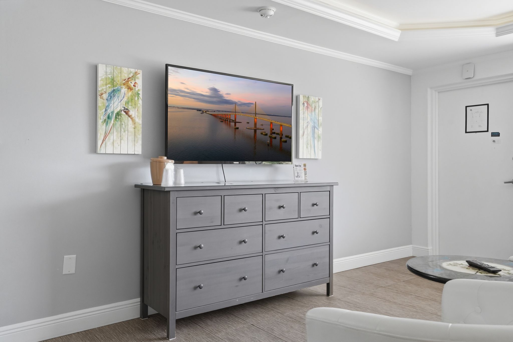 Uma sala de estar moderna com um armário cinza, uma TV de tela plana fixada na parede e um sofá branco.