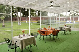 Uma área de refeições interna com mesas e cadeiras, janelas amplas e vista para o exterior.
