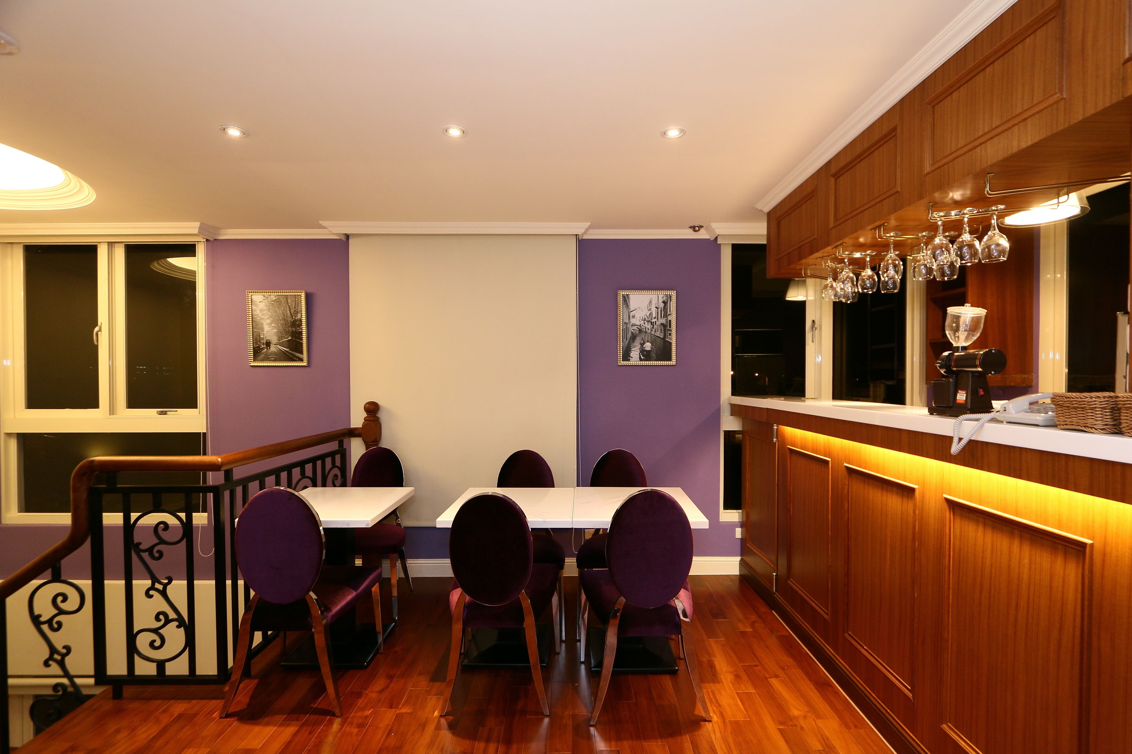 Uma área de jantar com mesa de madeira e cadeiras roxas, uma cozinha com armários de madeira e uma escada com corrimão.