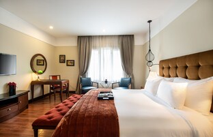 Quarto de hotel com uma cama grande, uma escrivaninha com cadeira, televisão e janela com cortinas.