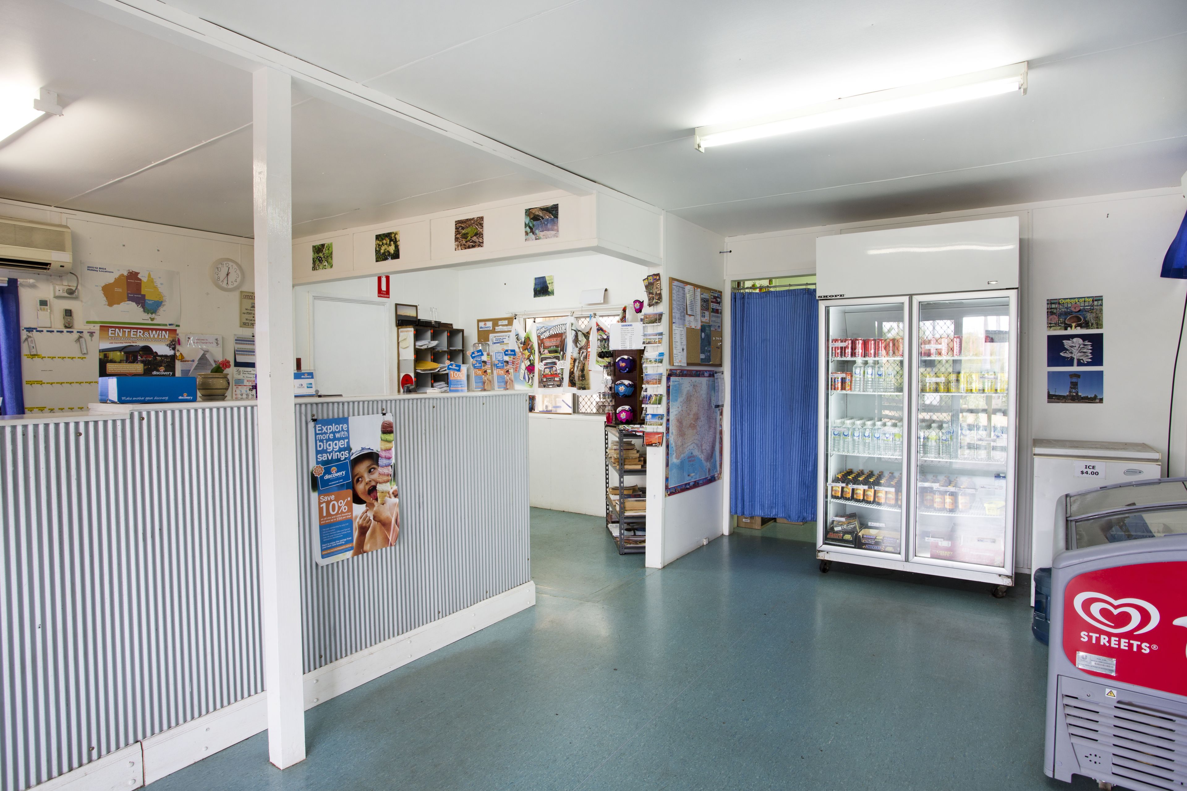 Uma loja limpa e bem iluminada, com balcão refrigerado, congelador e diversos produtos nas prateleiras.