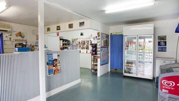 Uma loja limpa e bem iluminada, com balcão refrigerado, congelador e diversos produtos nas prateleiras.
