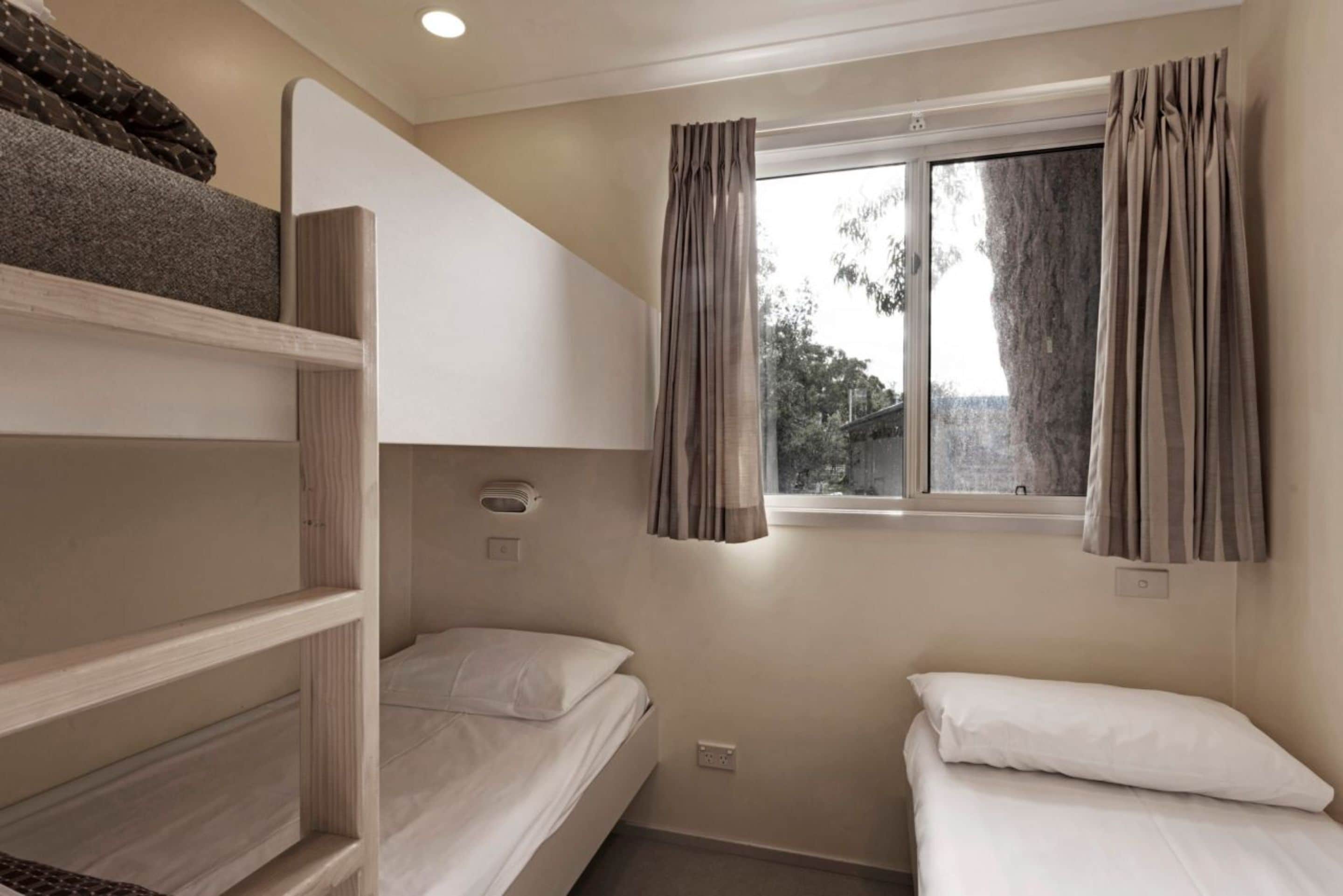 Quarto compacto com beliches, janela com cortinas e uma pequena mesa de cabeceira.