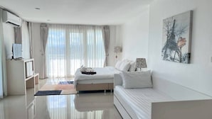 Quarto de hotel moderno com cama, sofá, escrivaninha e uma janela grande com cortinas.