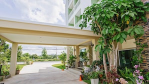 Entrada de hotel com galeria coberta, plantas em vasos e vista para o verde ao redor.