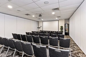 Uma sala de conferências com fileiras de cadeiras, um projetor e uma tela.