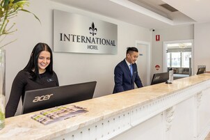 Uma receção do HOTEL INTERNACIONAL com design moderno, um sinal acima indicando o nome do hotel e um computador no balcão.
