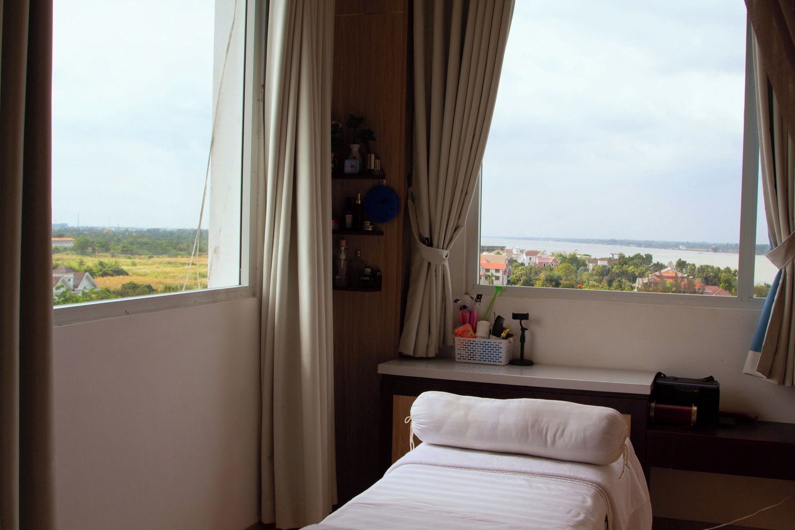 Quarto de hotel com cama, escrivaninha e vista para um rio e prédios.