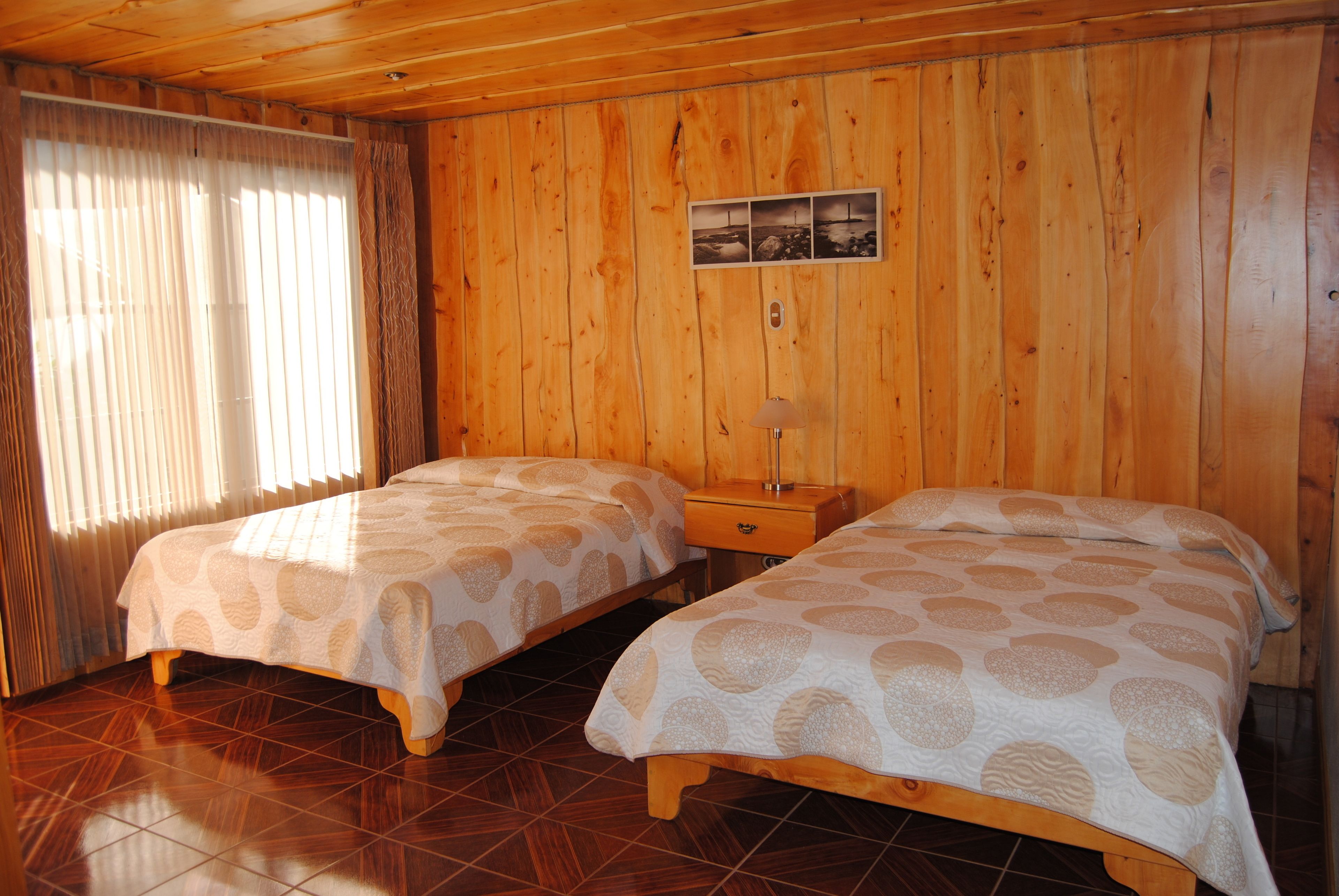 Quarto com painéis de madeira, duas camas, um criado-mudo e uma janela com cortinas.