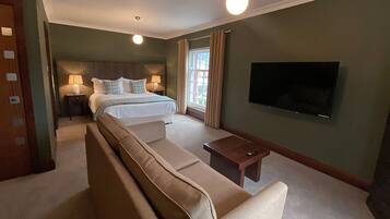 Quarto de hotel com uma cama grande, um sofá, uma TV e uma escrivaninha.