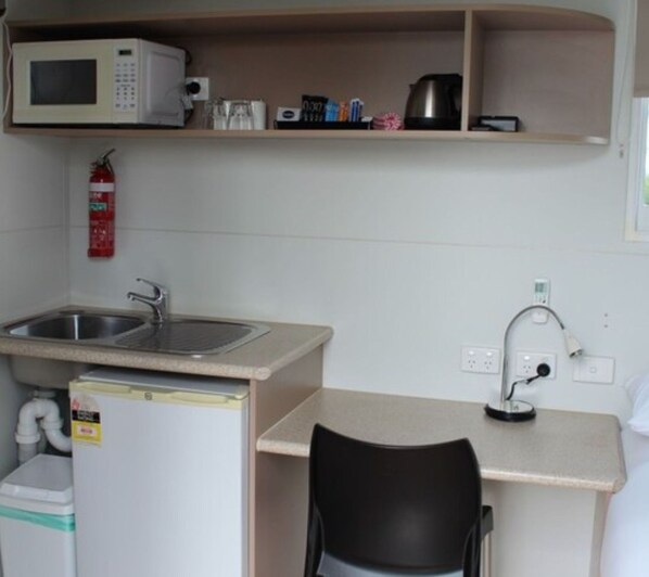 Uma cozinha compacta equipada com micro-ondas, pia e pequeno frigorífico.