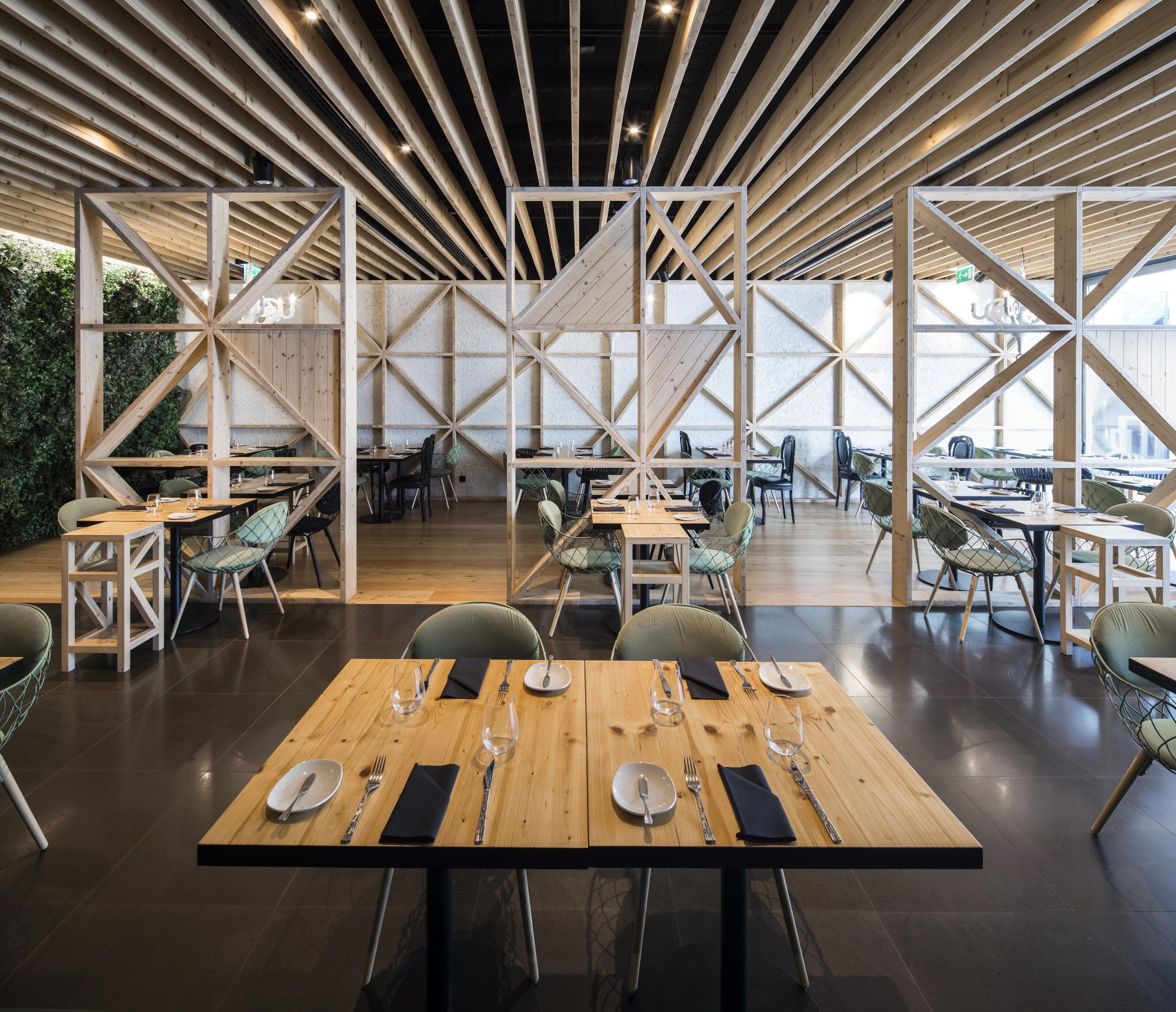Restaurante moderno com vigas de madeira aparentes e teto alto. Mesas dispostas em um ambiente espaçoso, com cadeiras.