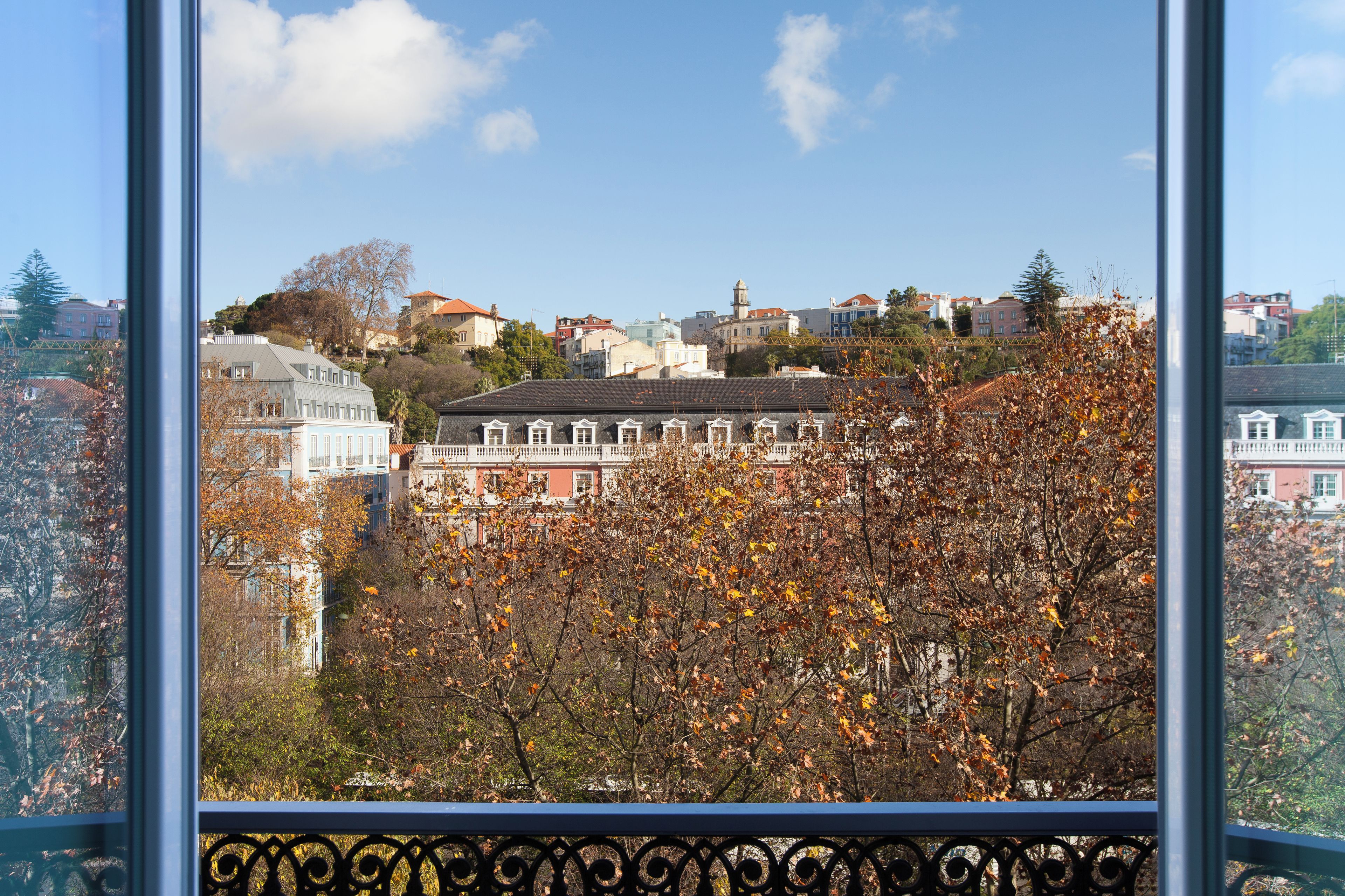 Vista pela janela de um horizonte urbano com edifícios, árvores e céu limpo.