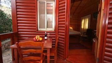 Uma cabana de madeira com área de refeições, uma janela e um quarto visível por uma porta aberta.