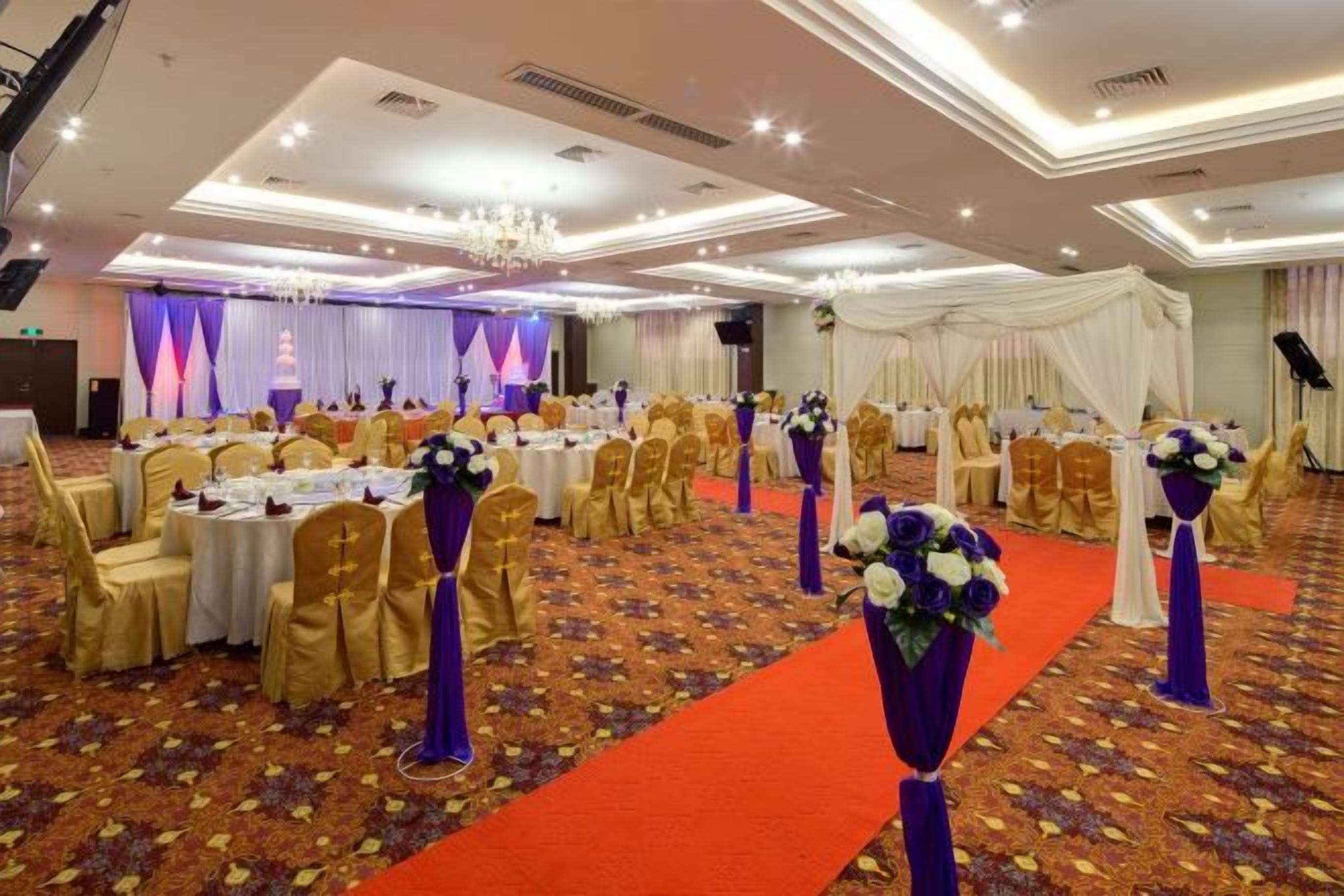 Uma sala de banquetes com mesas redondas, cadeiras douradas e um tapete vermelho.