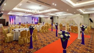 Uma sala de banquetes com mesas redondas, cadeiras douradas e um tapete vermelho.