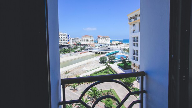 Vista de uma varanda com vista para uma área costeira, edifícios, uma praia e um porto de iates.