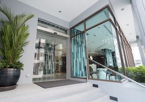 Entrada de um edifício moderno com porta de vidro, planta em vaso e escadaria que dá acesso ao interior.