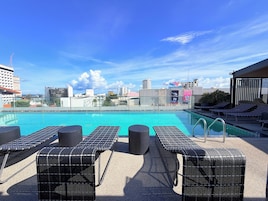 Piscina no terraço com espreguiçadeiras e vista para a cidade.