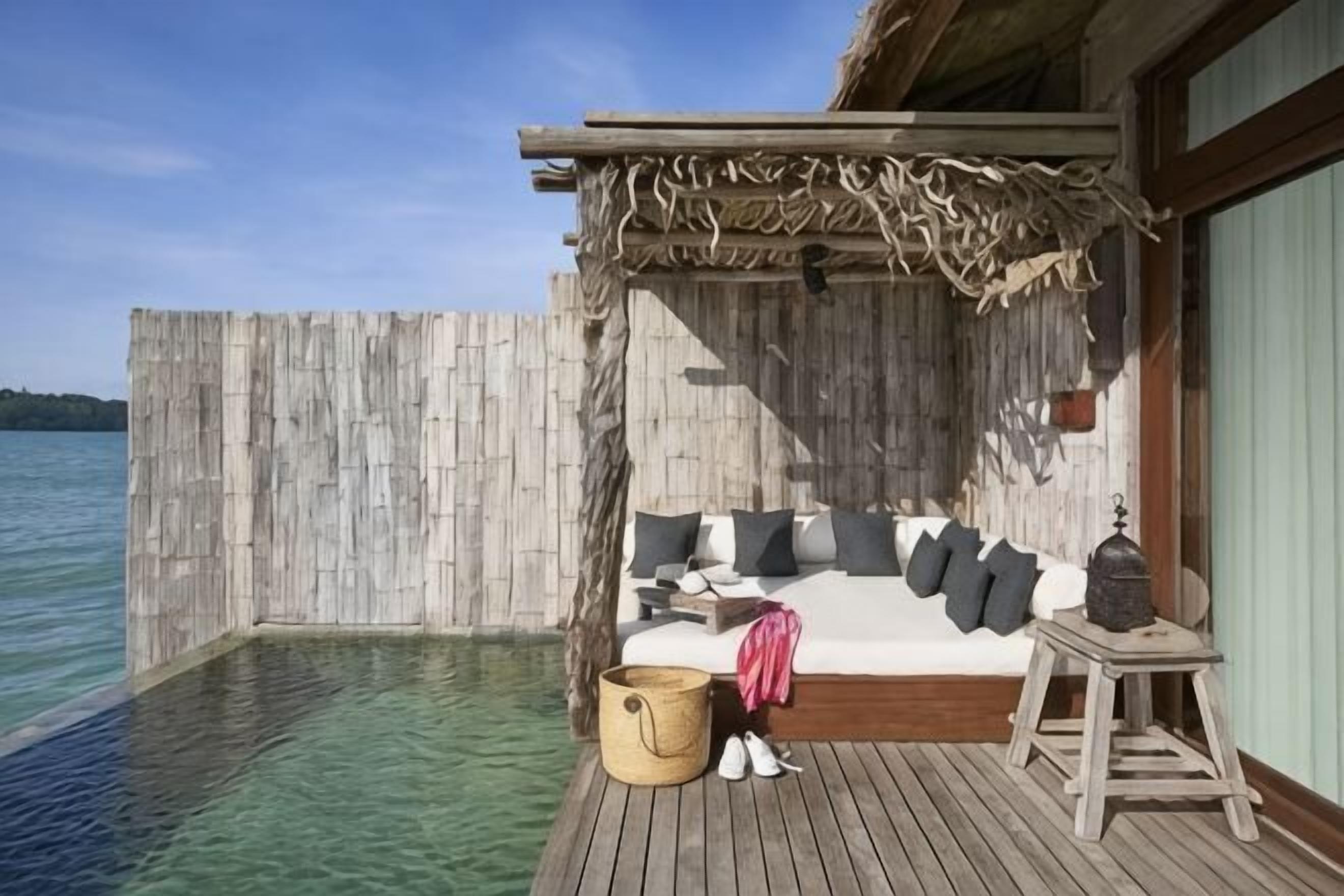 Bungalôs sobre a água com deck de madeira, sofá com almofadas, um balde e uma pequena mesa.