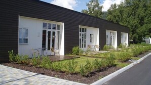 Um edifício moderno com três divisões, cada uma com porta e janelas. Possui áreas externas com mesas e cadeiras.