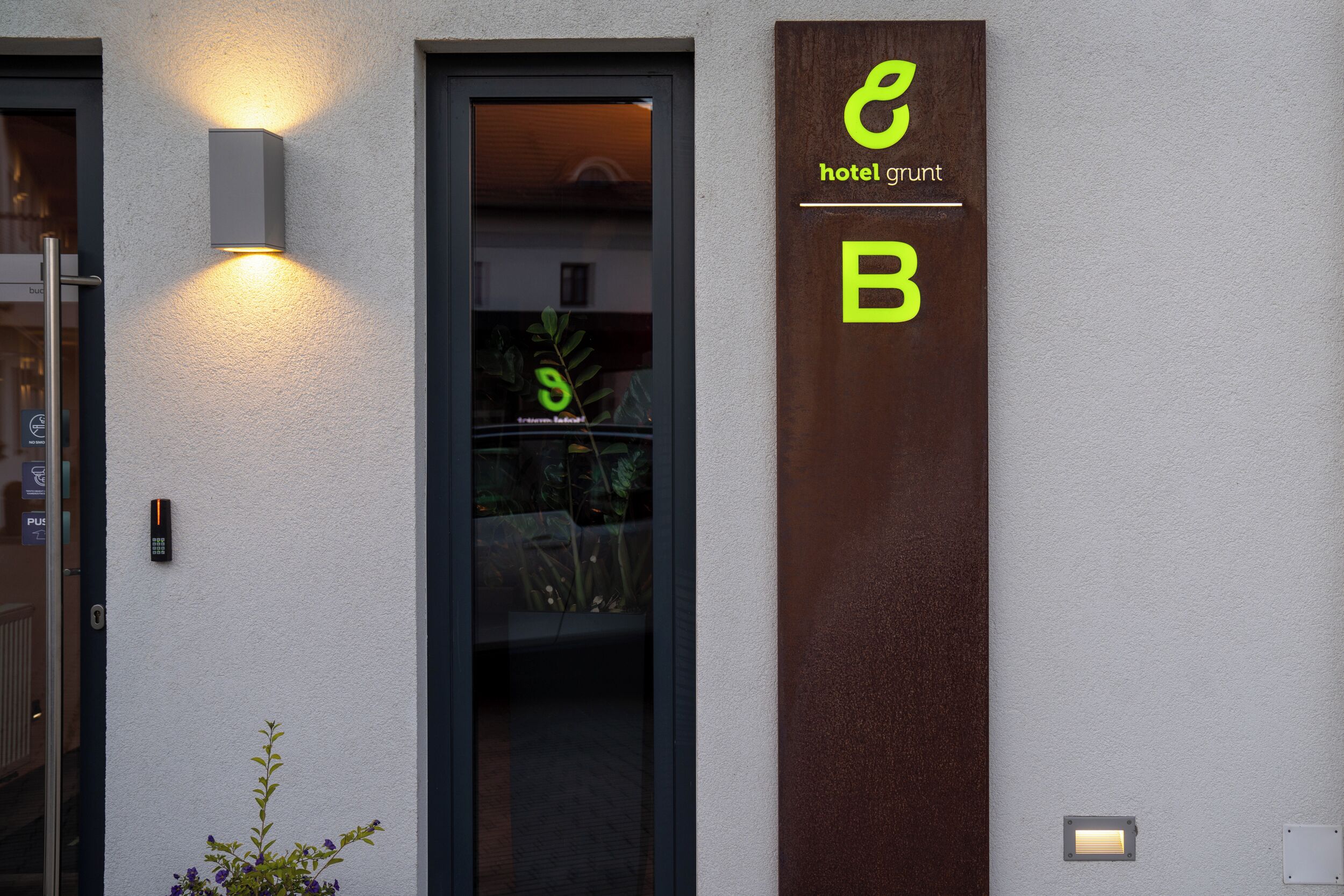 Entrada de hotel com design moderno, incluindo uma placa com 'hotel grunt' e uma porta com painel de vidro.