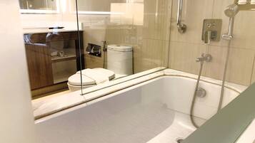 Um banheiro moderno com chuveiro em gabinete de vidro, vaso sanitário branco e toucador de madeira.