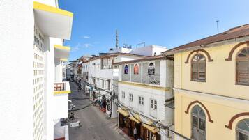 Uma rua estreita ladeada por edifícios de vários andares, alguns com varandas e outros com lojas no térreo.