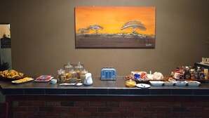 Buffet de café da manhã com diversos alimentos e uma pintura de árvores na parede.