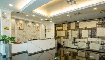 Uma área de recepção de hotel com paredes de mármore, balcão de recepção e uma exposição de certificados emoldurados.