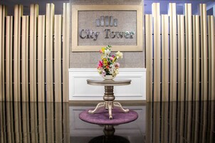 Uma área de recepção com uma placa indicando "City Tower", uma mesa redonda com um arranjo floral e um tapete decorativo.