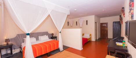 Quarto de hotel com uma cama, uma escrivaninha e uma cadeira. Há uma televisão na parede.