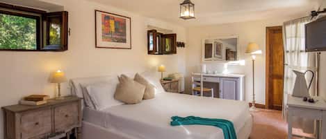 Quarto com cama, mesas de cabeceira, espelho, televisão e janela com cortinas.