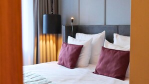 Quarto de hotel com uma cama grande, cabeceira com luminária e janela com cortinas.